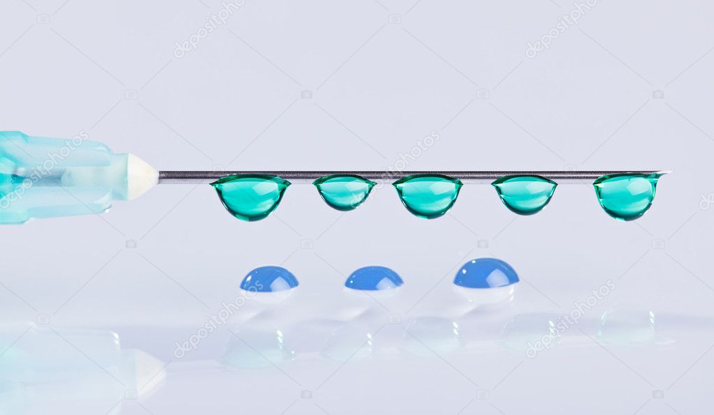 Syringe needle with green fluid drops on droplets water backgrou ...