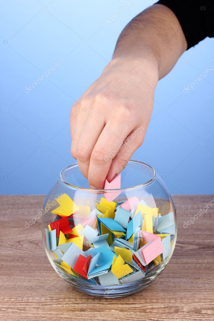Hand throwing piece of paper for lottery on wooden table on blue ...