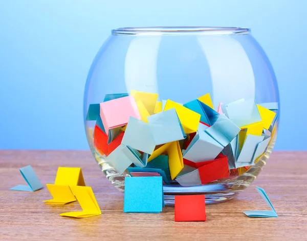 Pieces of paper for lottery in vase on wooden table on blue background ...