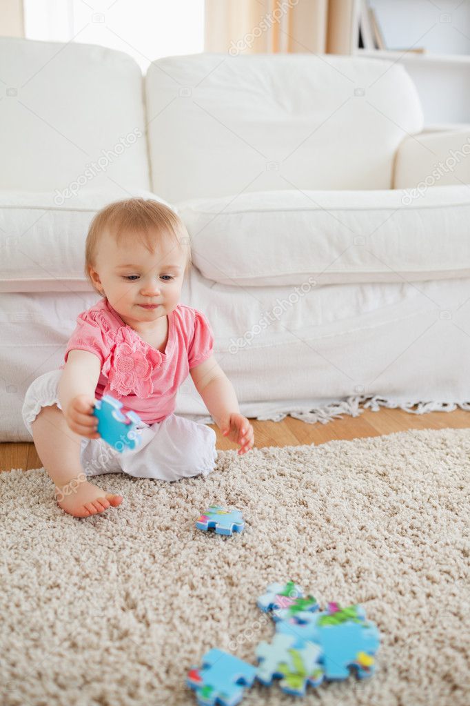 Lovely blond baby playing with puzzle pieces while sitting on a Stock ...